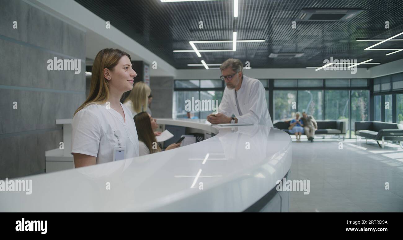 Female administrator stands at reception desk in clinic lobby area ...
