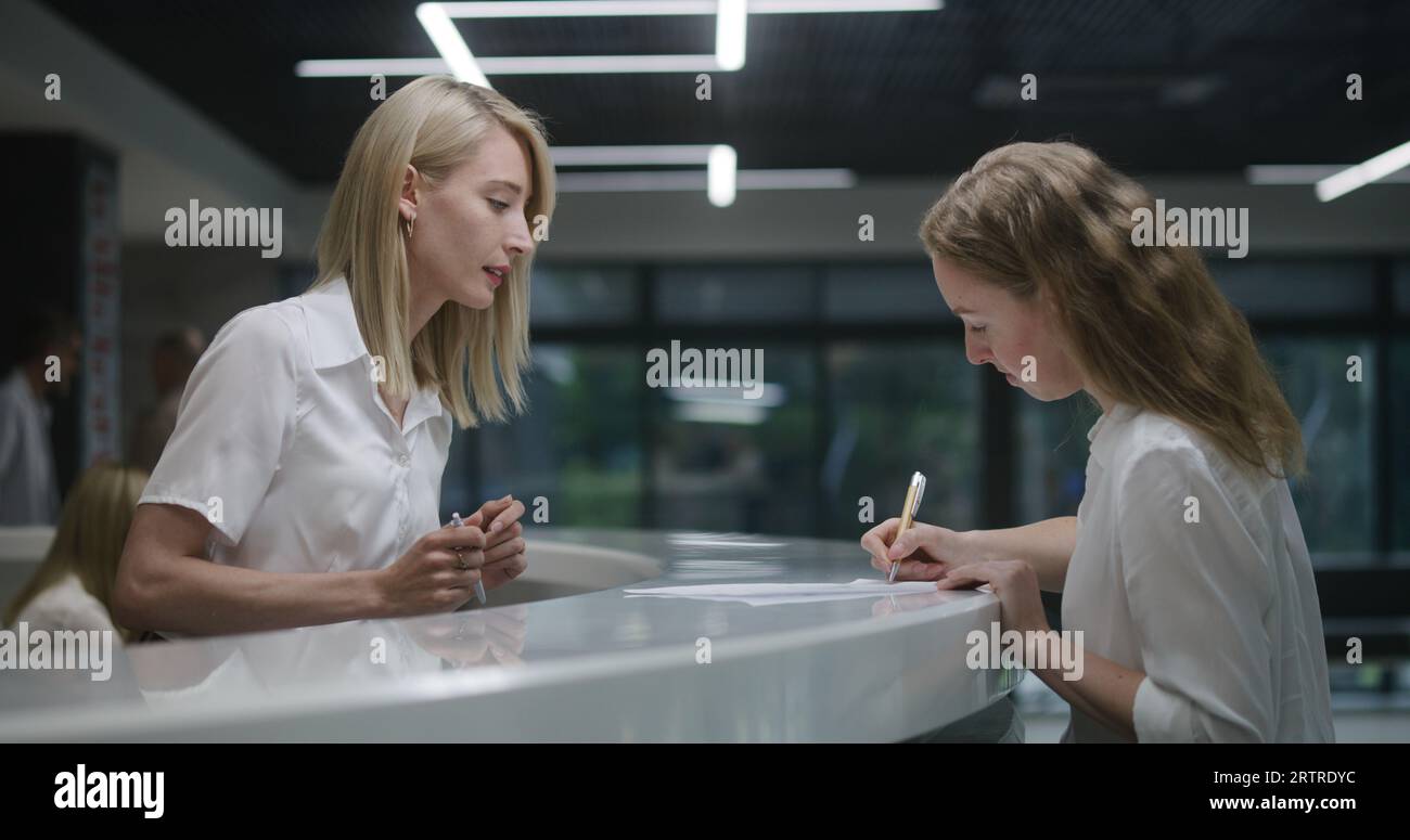 Female administrator talks with patient at reception desk in clinic ...