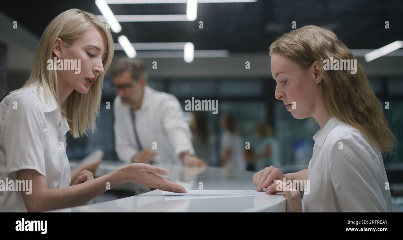 Female administrator talks with patient at reception desk in clinic ...