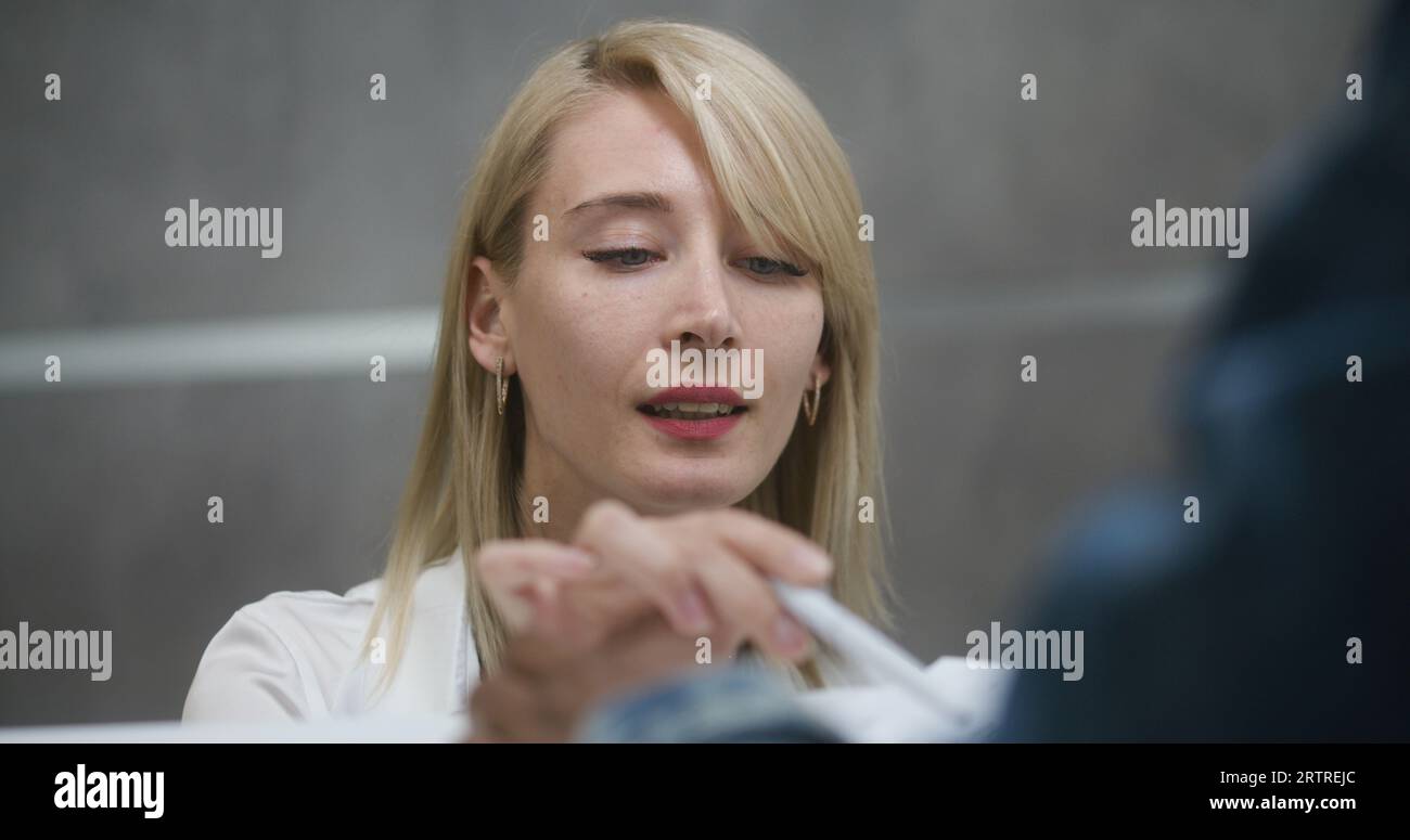 Female administrator talks with patient at reception desk in clinic ...