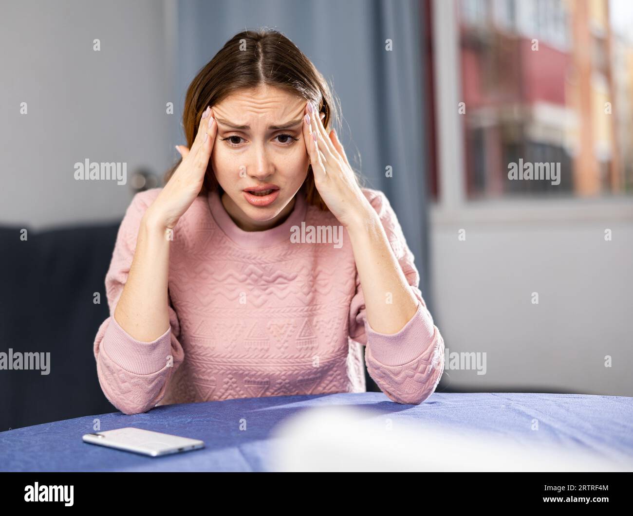 Portrait of a frustrated young woman sitting at a table Stock Photo - Alamy