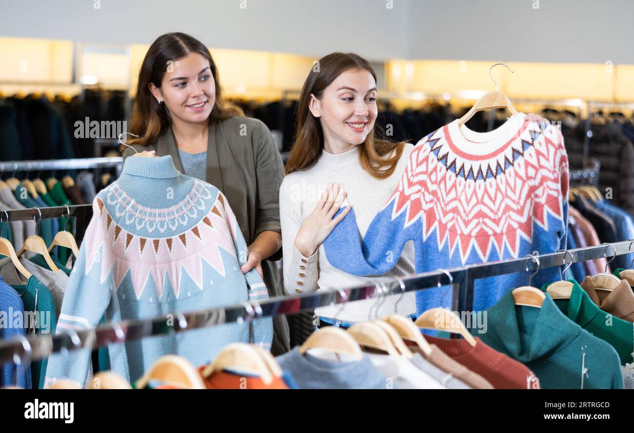 Positive young women friends choosing winter sweater in fashion store ...