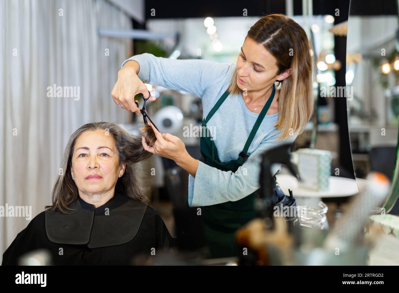 Woman hair stylist making haircut to aged female client Stock Photo - Alamy
