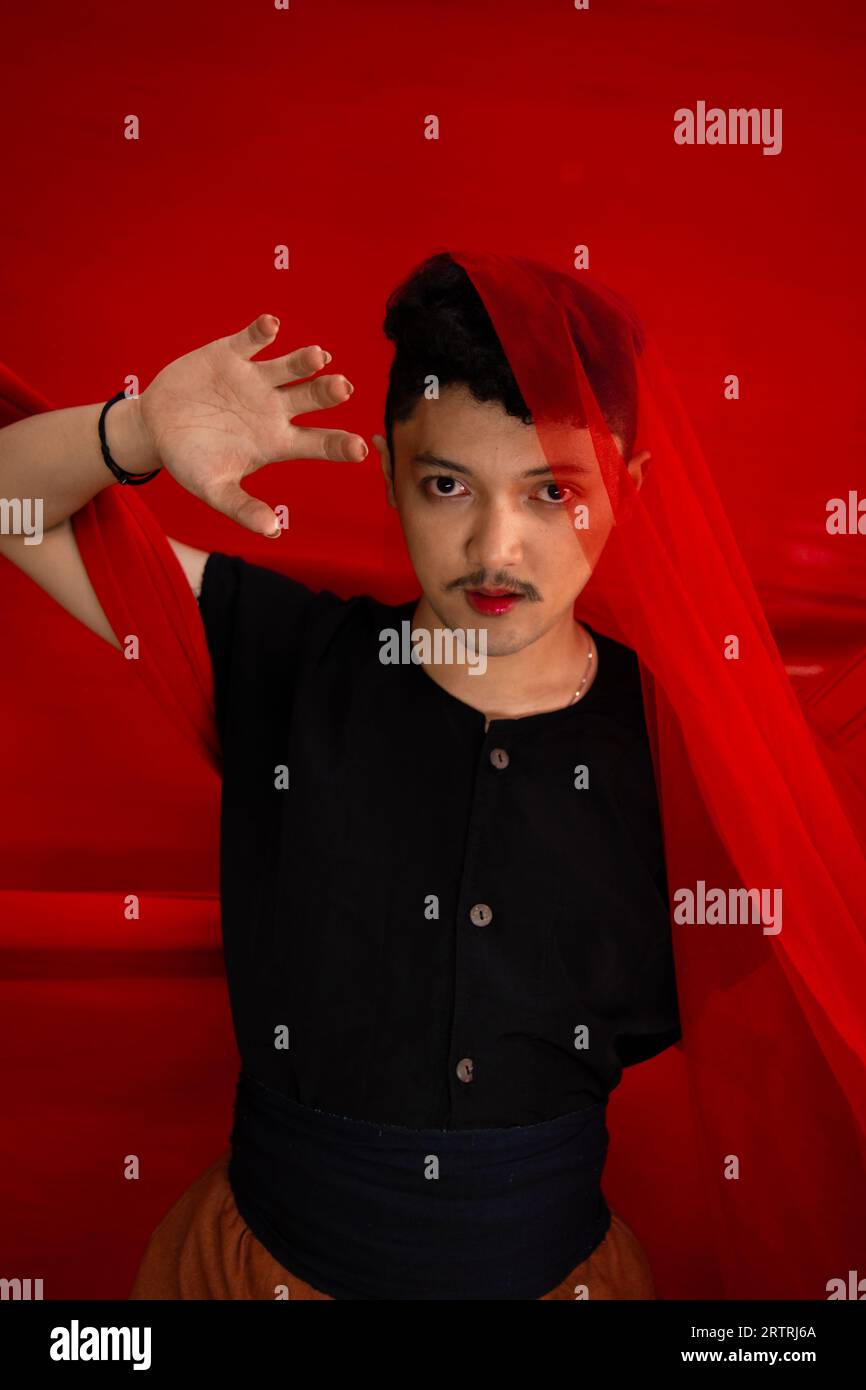 an Asian man in a black shirt covering his face with a red cloth with a ...