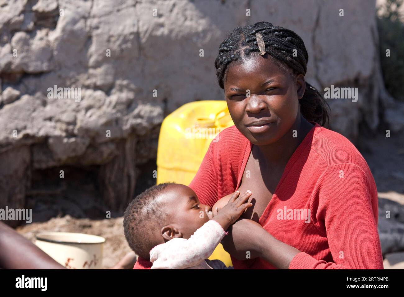 African woman breastfeeding her baby, sitting in front of mud hut ...