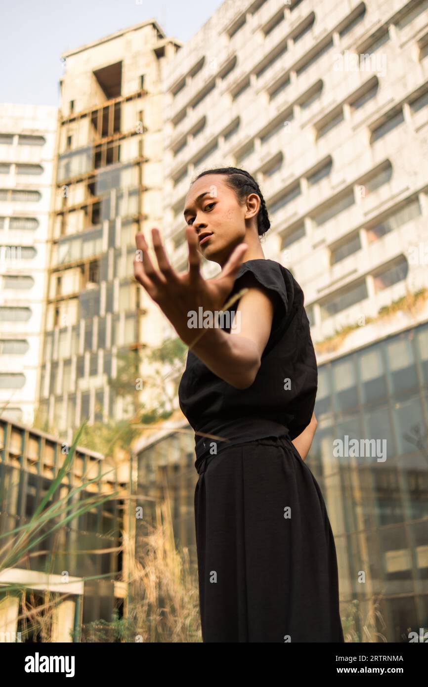 an Asian man posing in a black costume in front of a tall, towering ...