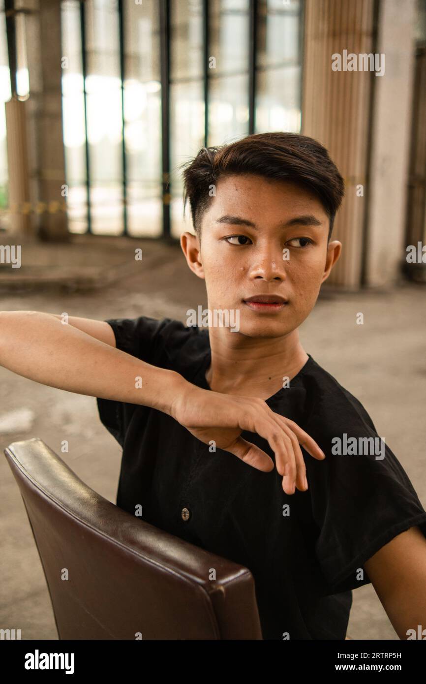 an Asian man posing on a brown leather chair while wearing black pants ...