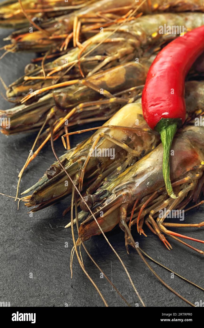 Raw unpeeled king prawns with a red chilli pepper on black slate Stock Photo - Alamy