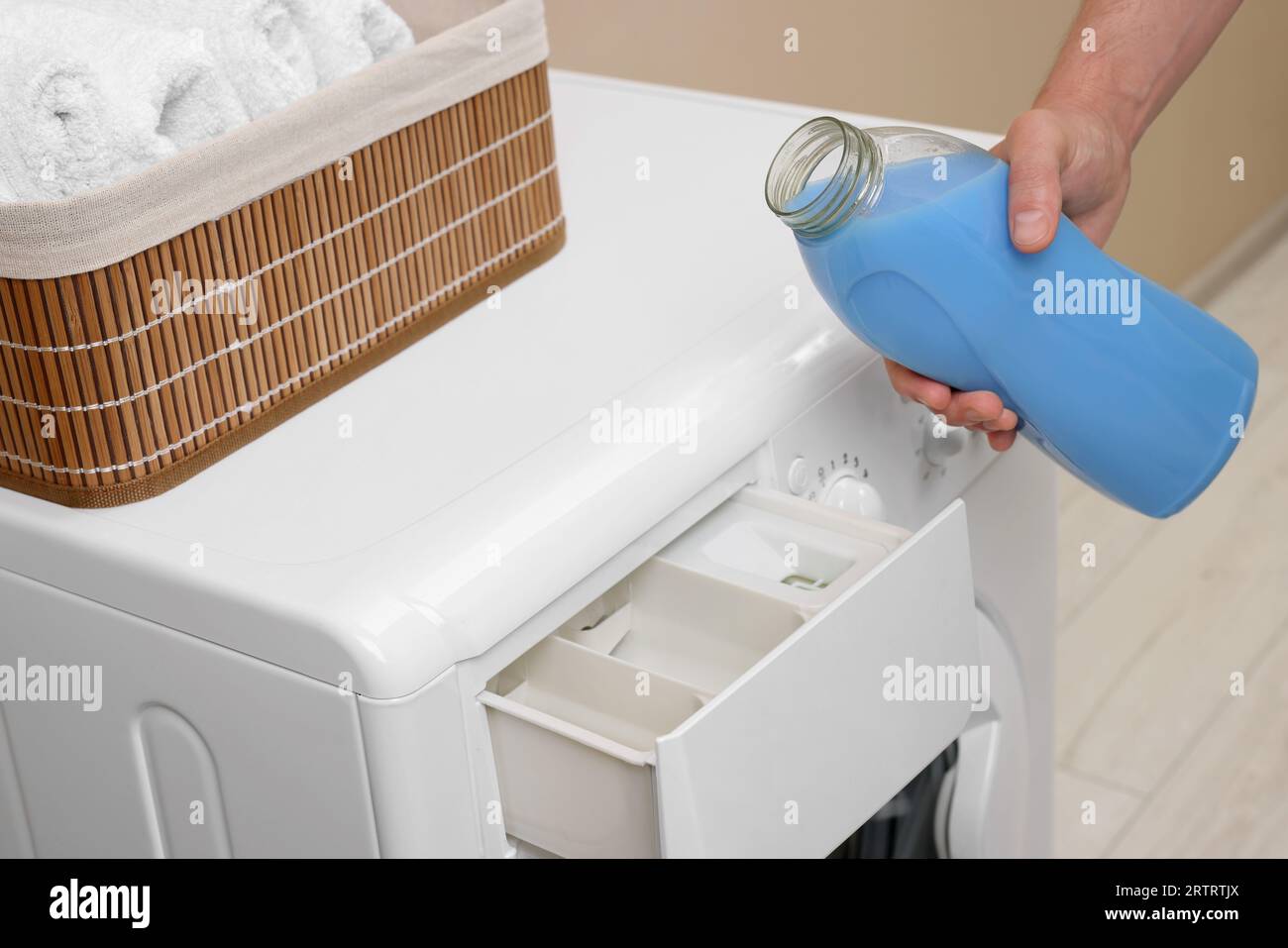 Man pouring fabric softener from bottle into washing machine indoors ...
