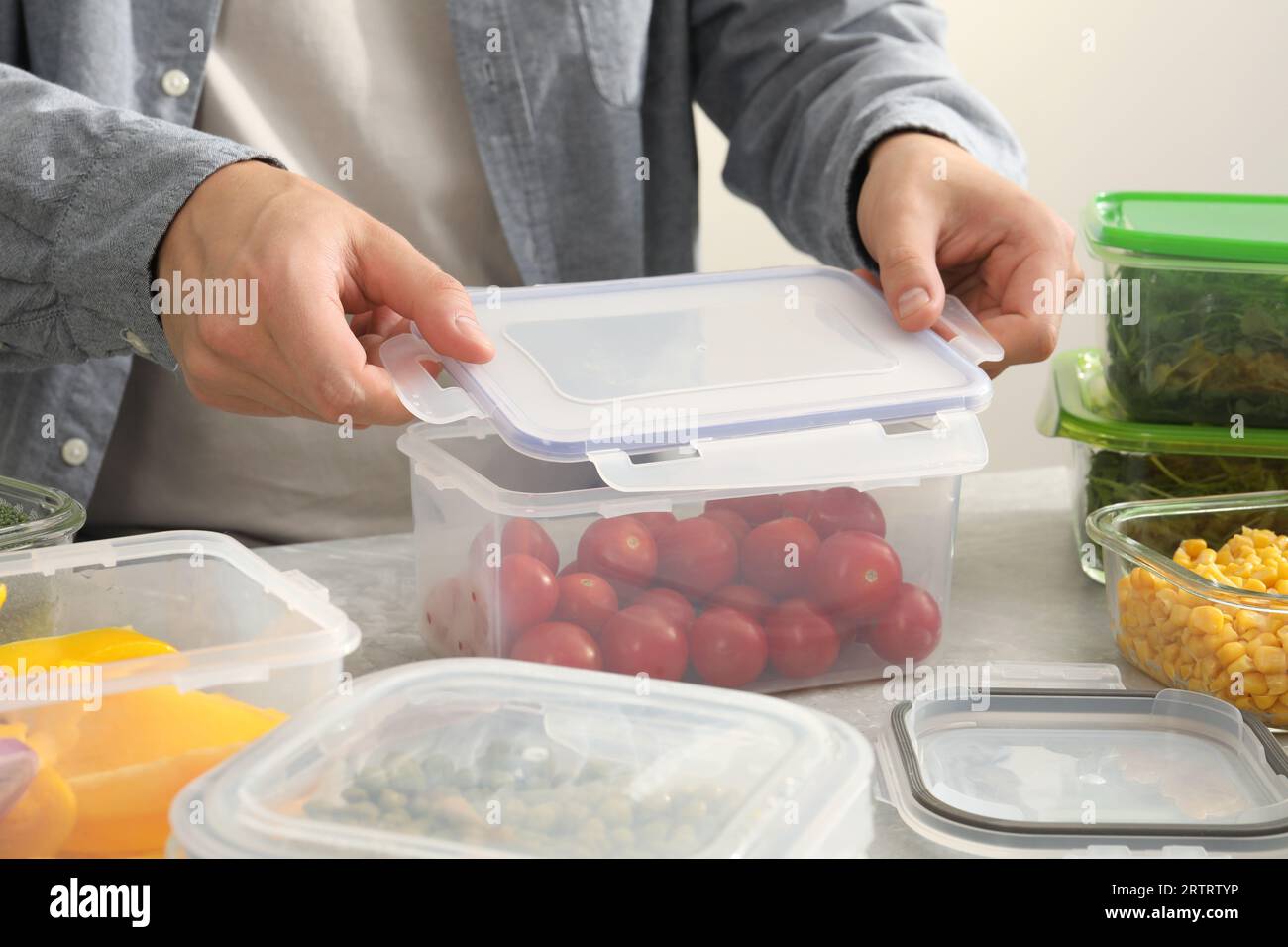 Man closing plastic container with lid at light grey marble table in ...