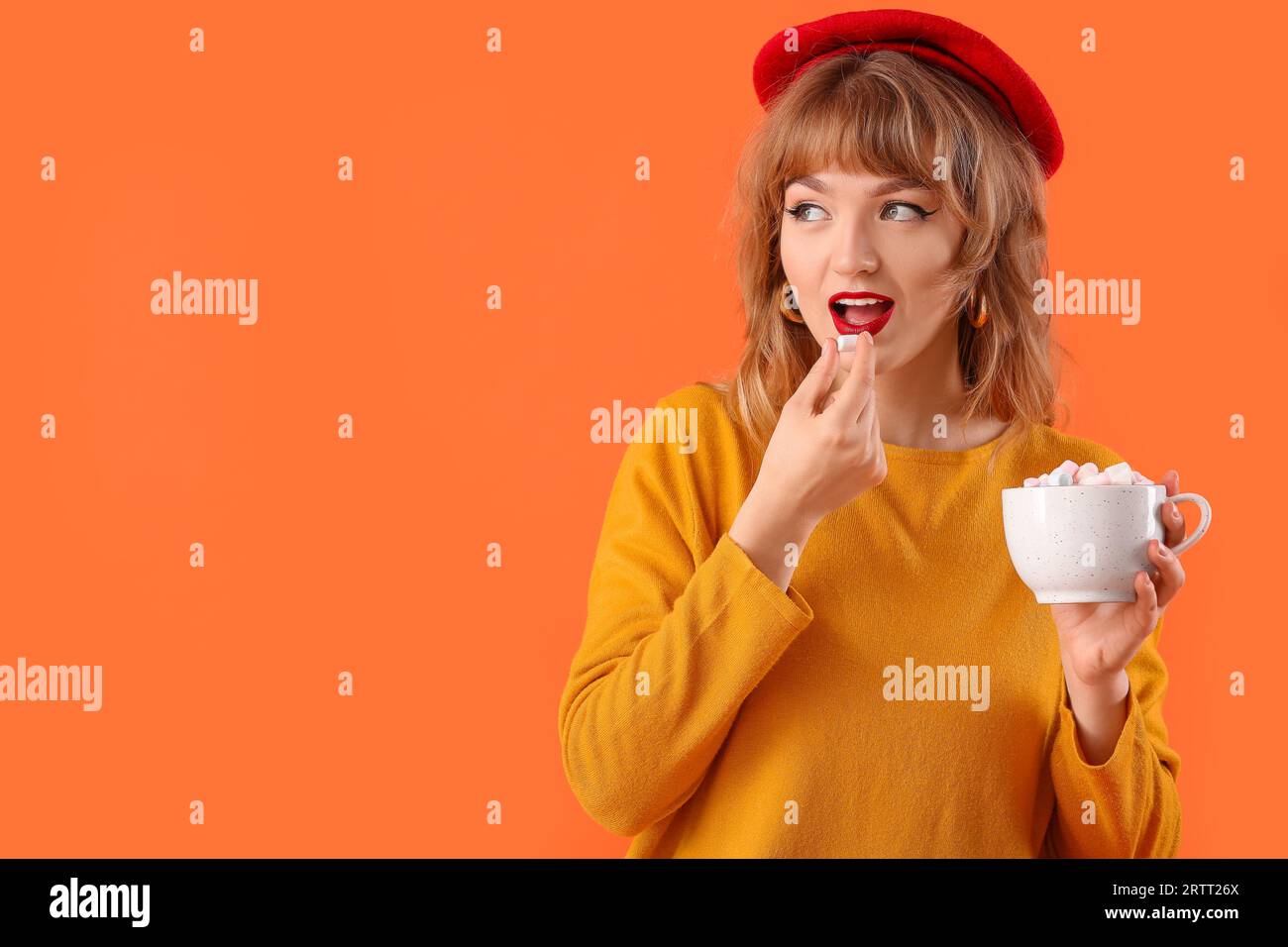 Stylish young woman in beret with cup of cocoa eating marshmallow on ...