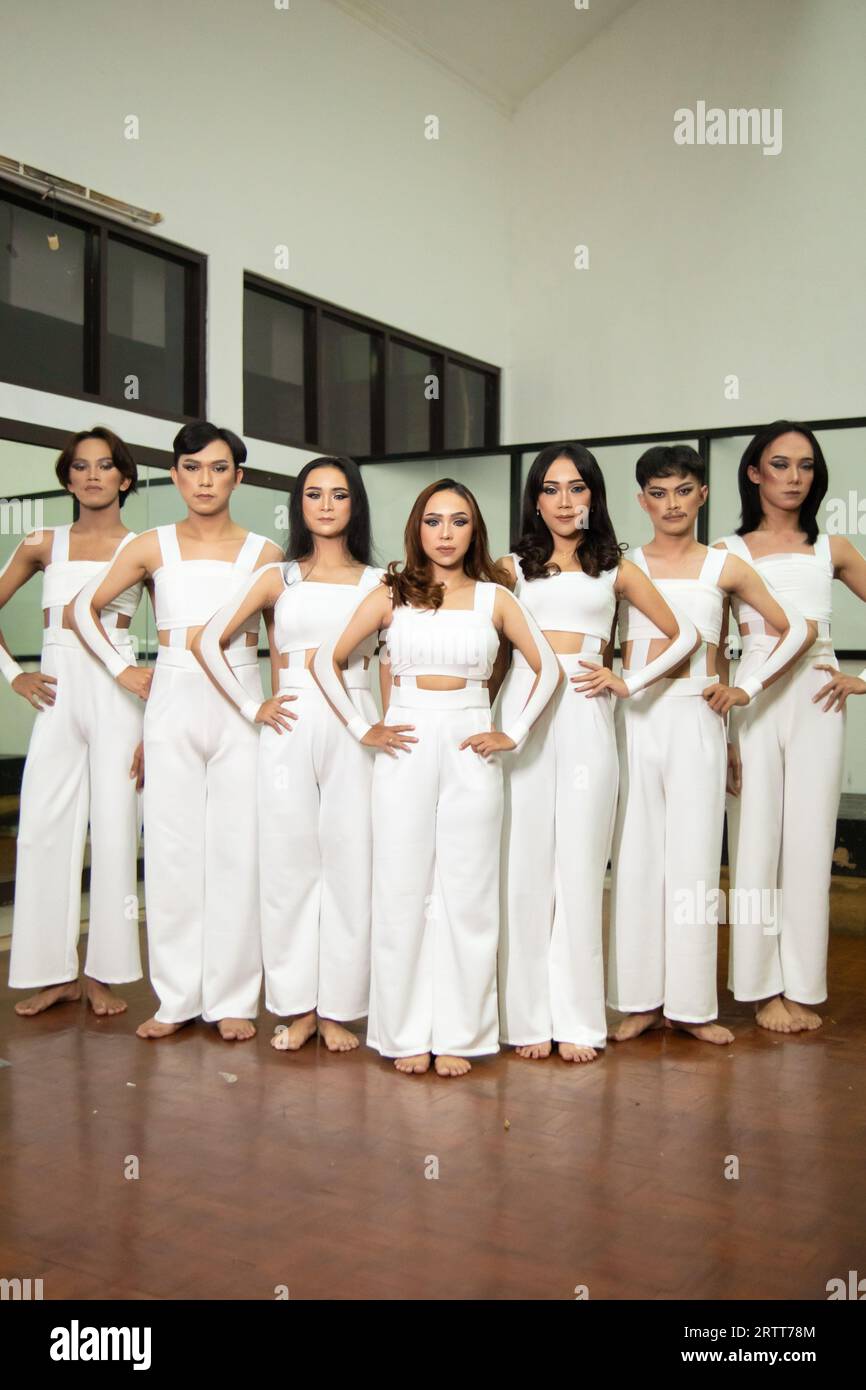 a group of Asian dancers stand side by side in white costumes in a room ...