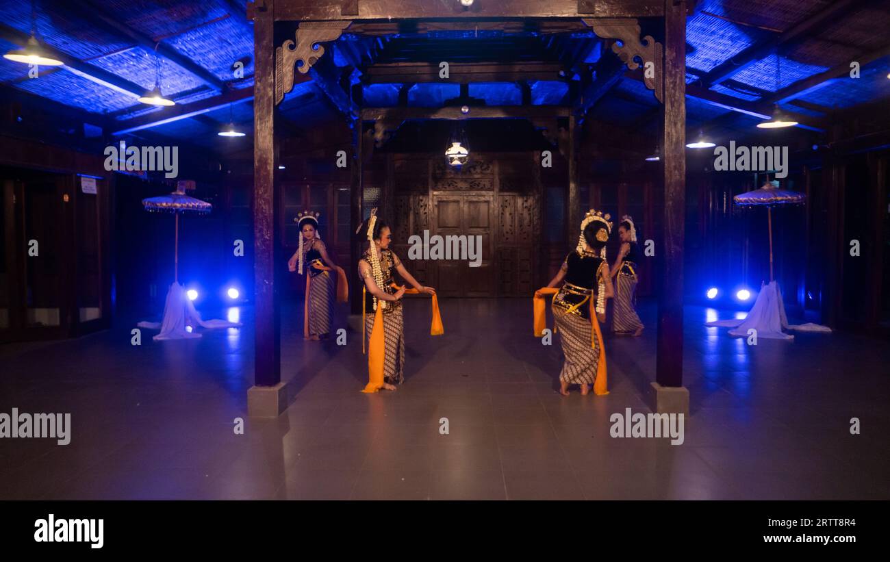 a group of Javanese dancers dances in a gazebo with brown wood at night ...