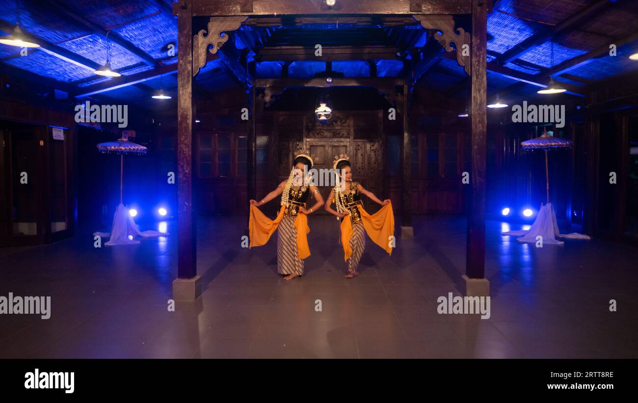 a group of Javanese dancers in yellow shawls dance in front of a blue ...