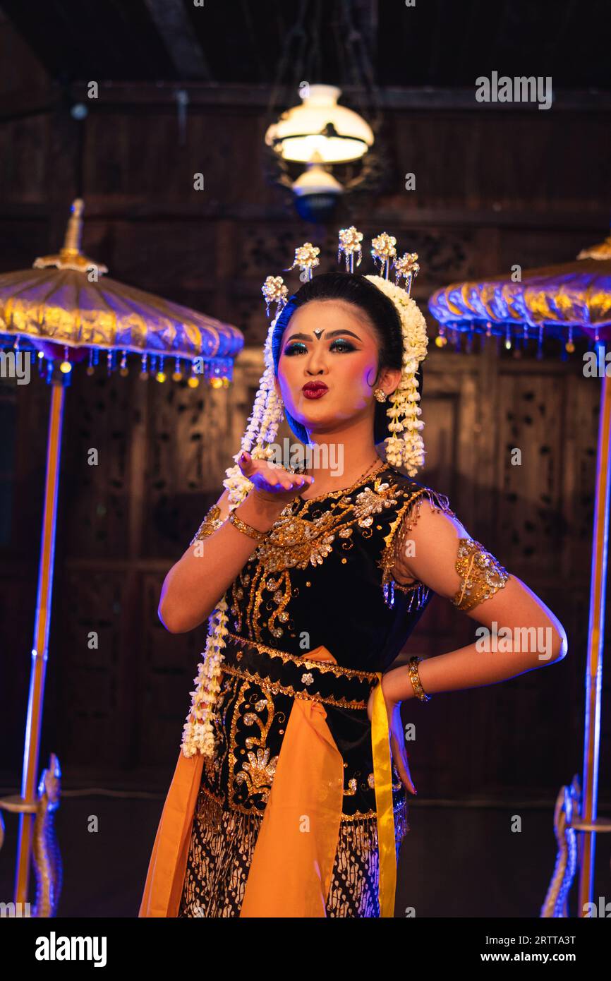 a Javanese dancer in jasmine and a yellow shawl takes selfies on stage ...