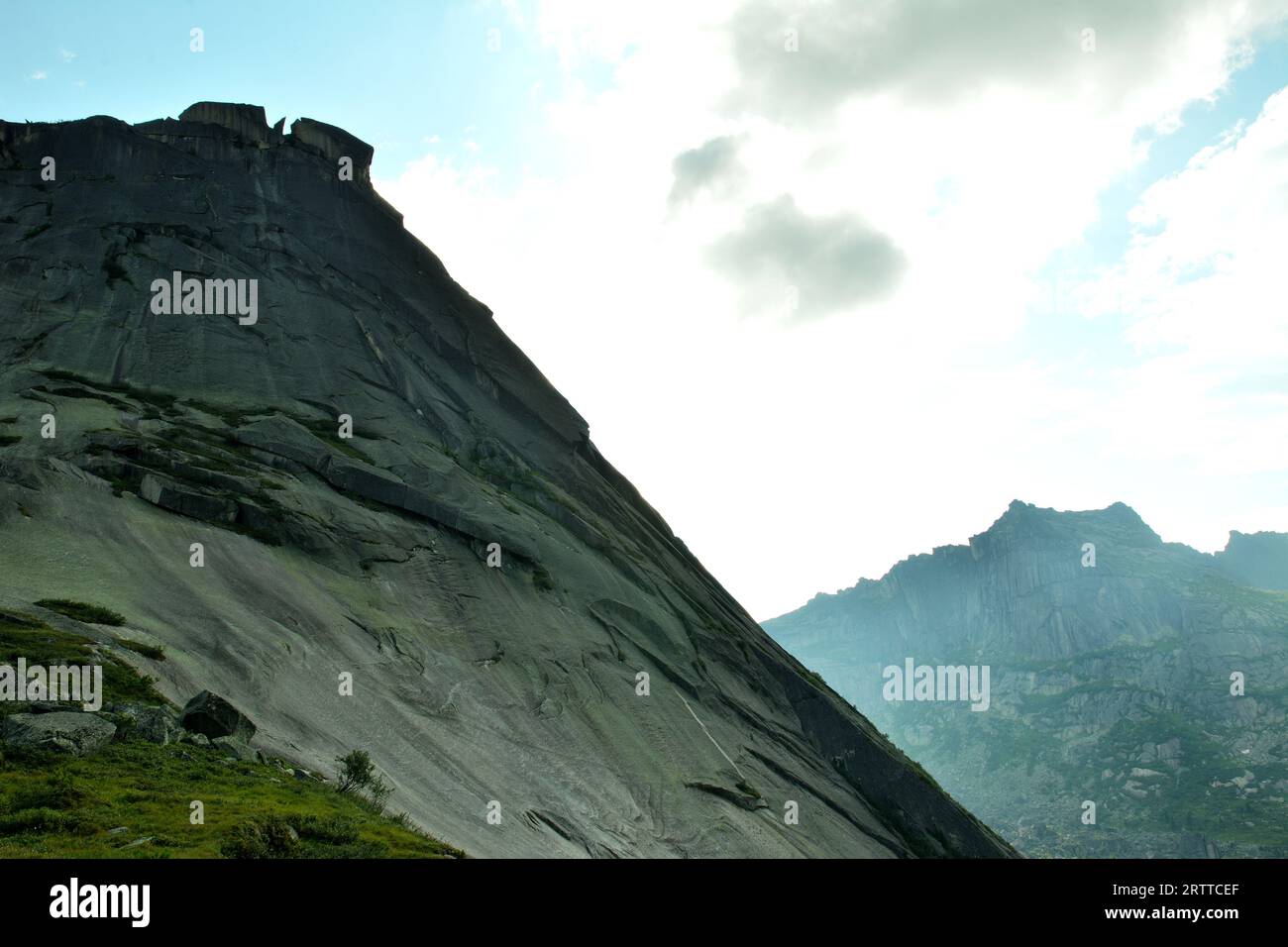 A very high sheer cliff with a flat slope on the edge of a mountain range on a sunny summer day ...