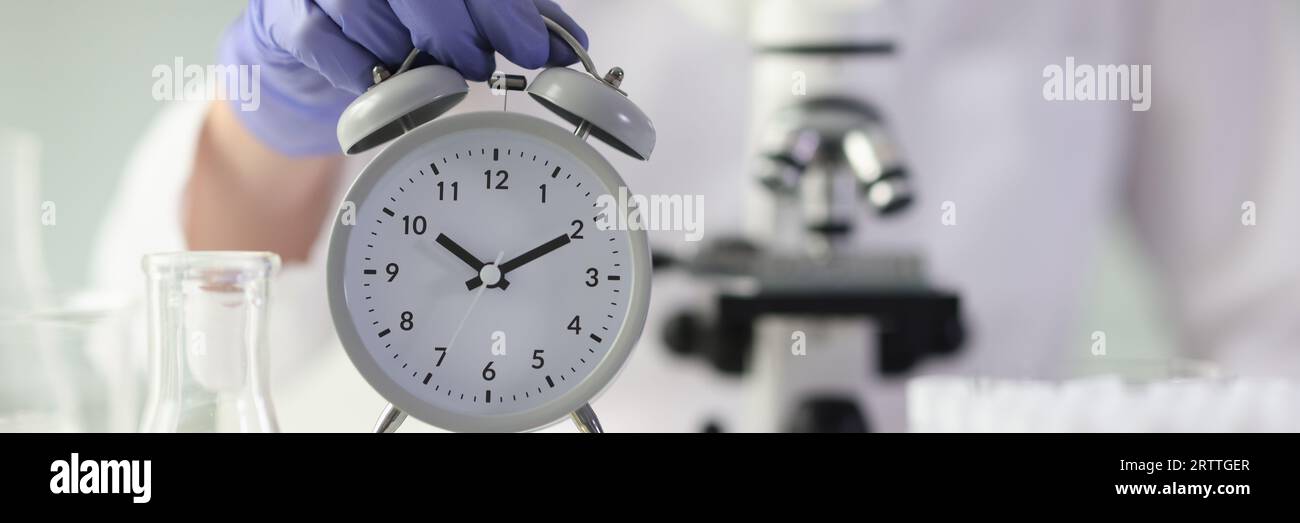 Scientist with test tubes, flask and microscope holds alarm clock in ...