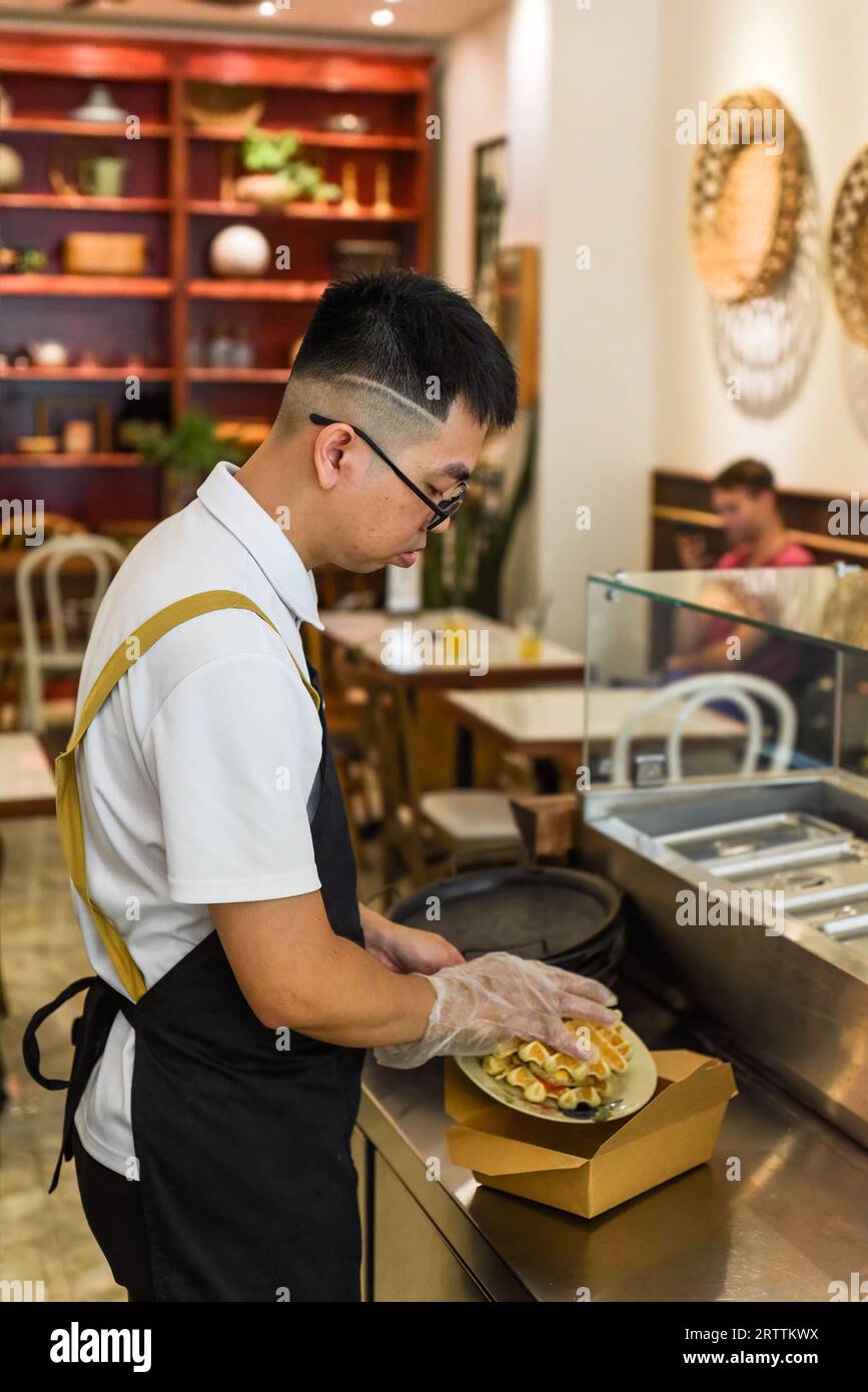Vietnamese man chef in uniform holding fresh baked belgian waffles with ...