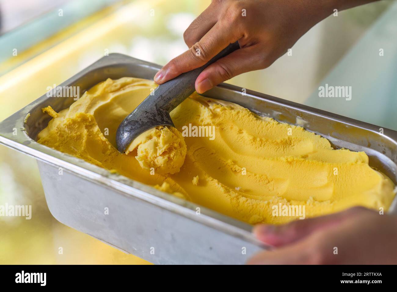 hand scooping a scoop of Passion fruit ice cream into a spoon in fridge ...