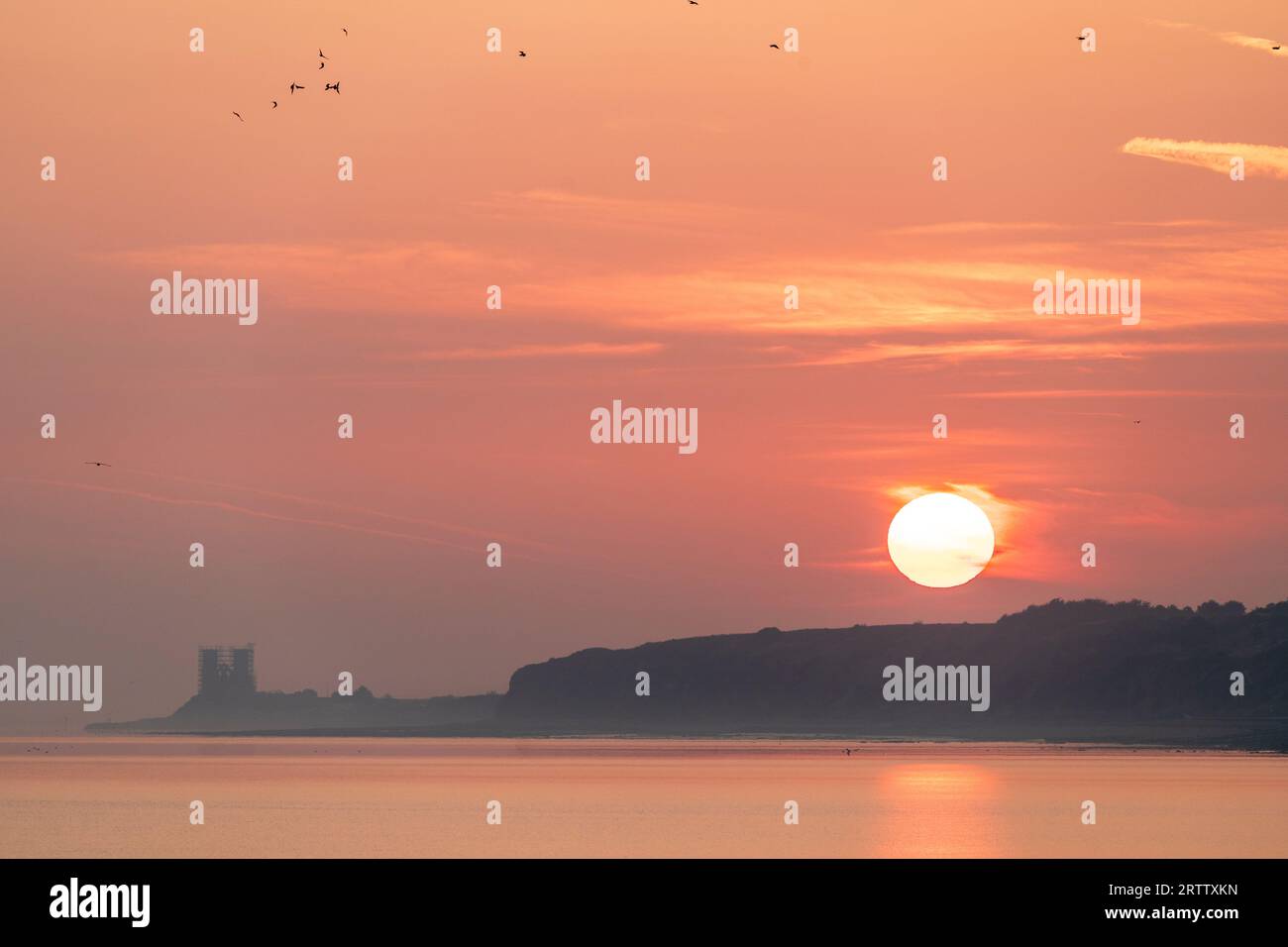 Sunrise over the coast at Reculver in Kent, with the silhouette of the ...