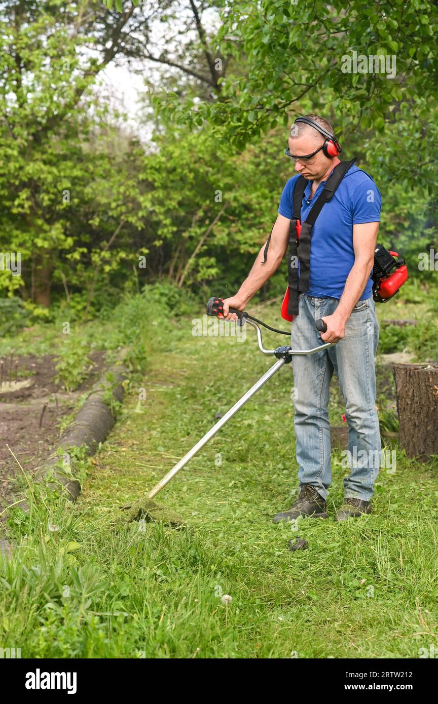 Man mowing tall grass with petrol lawn trimmer vertical photo Stock ...