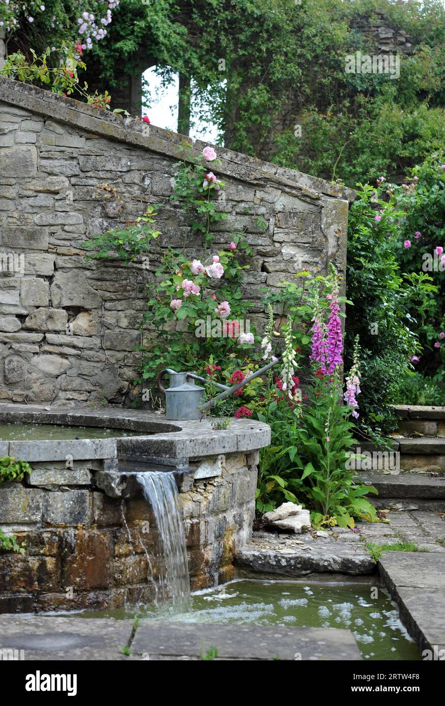 Watering can by a water feature in a walled garden, UK Stock Photo - Alamy