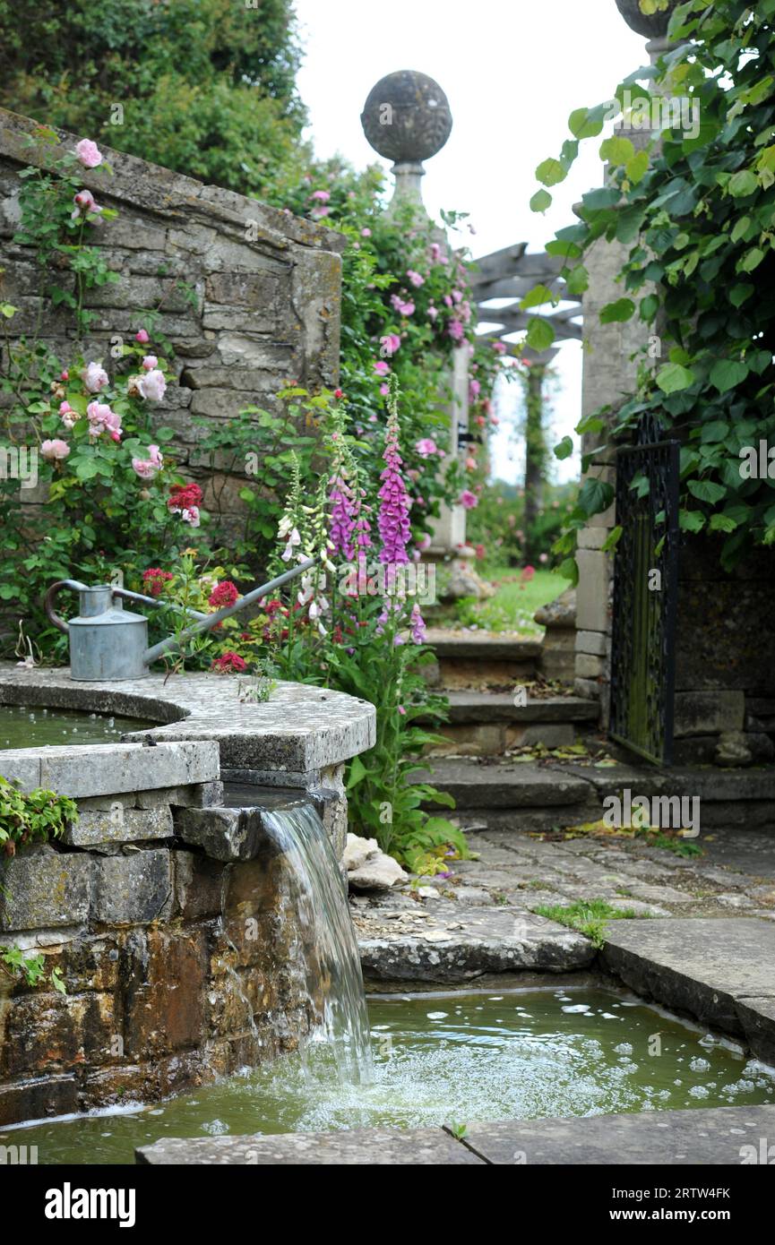 Watering can by a water feature in a walled garden, UK Stock Photo - Alamy