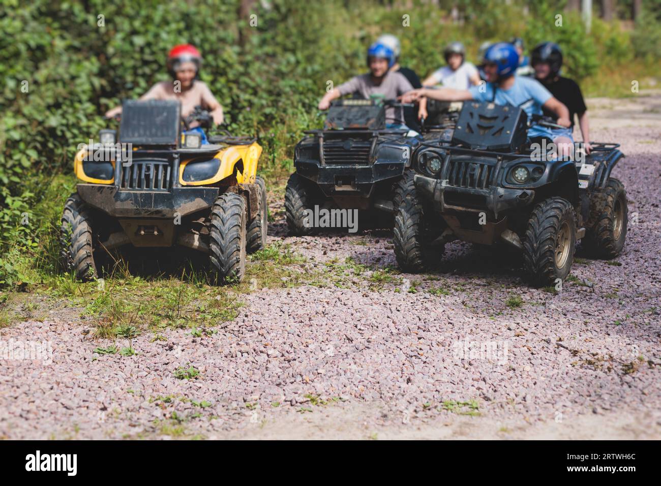 Group of riders riding ATV vehicle crossing forest rural road, process ...
