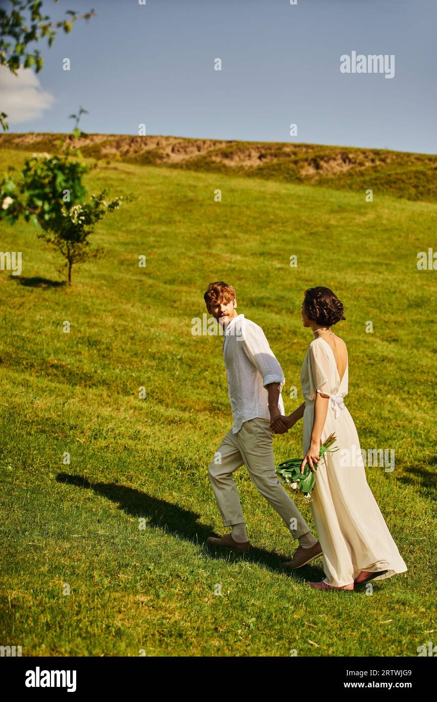 just married interracial couple in white wedding attire holding hands ...