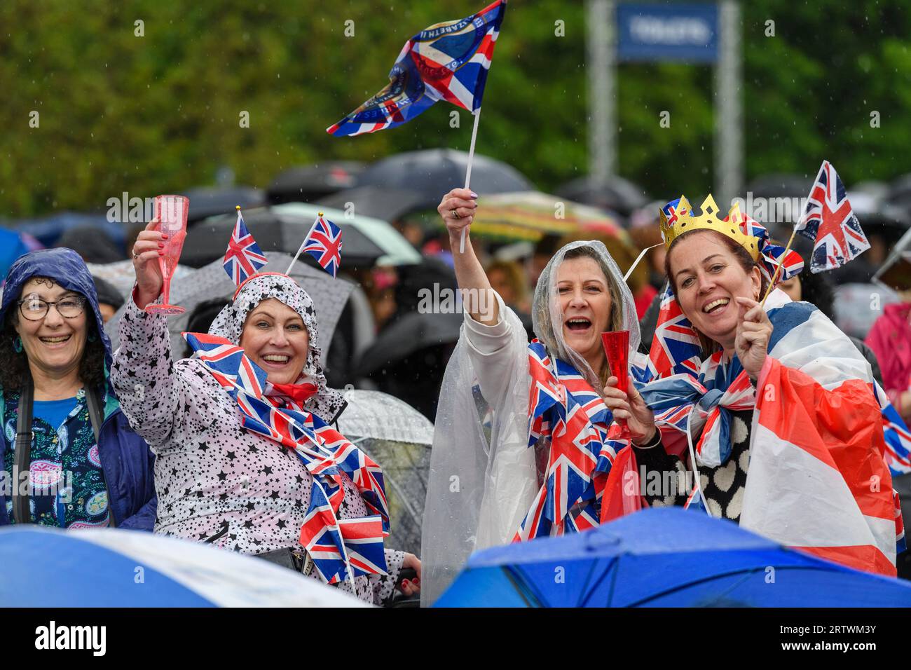 Three women waving Union Jack flags as they brave the rain to watch the ...