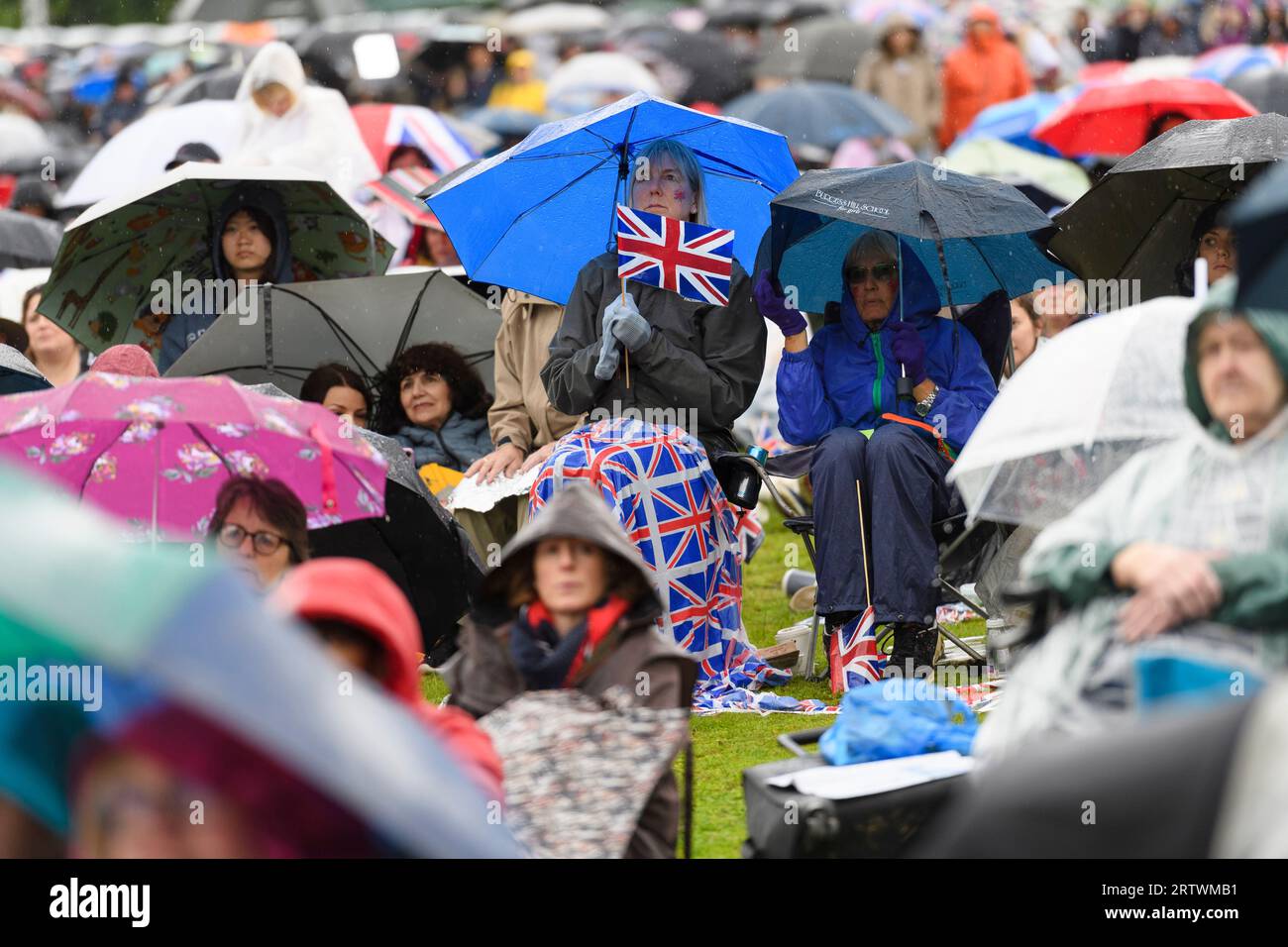 A woman sheltering from the rain under an umbrella holds a Union Jack ...