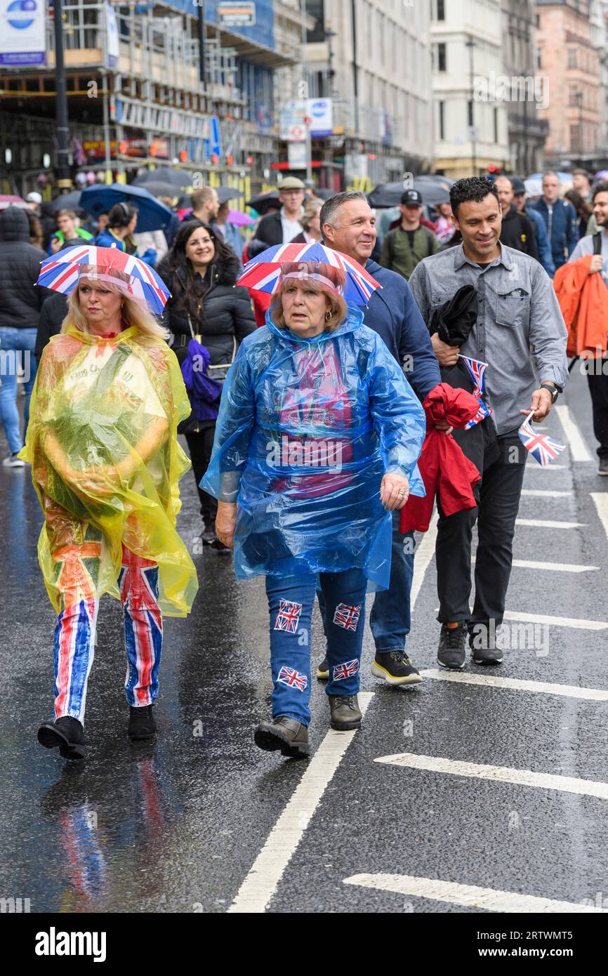 Two women in Union Jack outfits walking along Piccadilly in the rain ...
