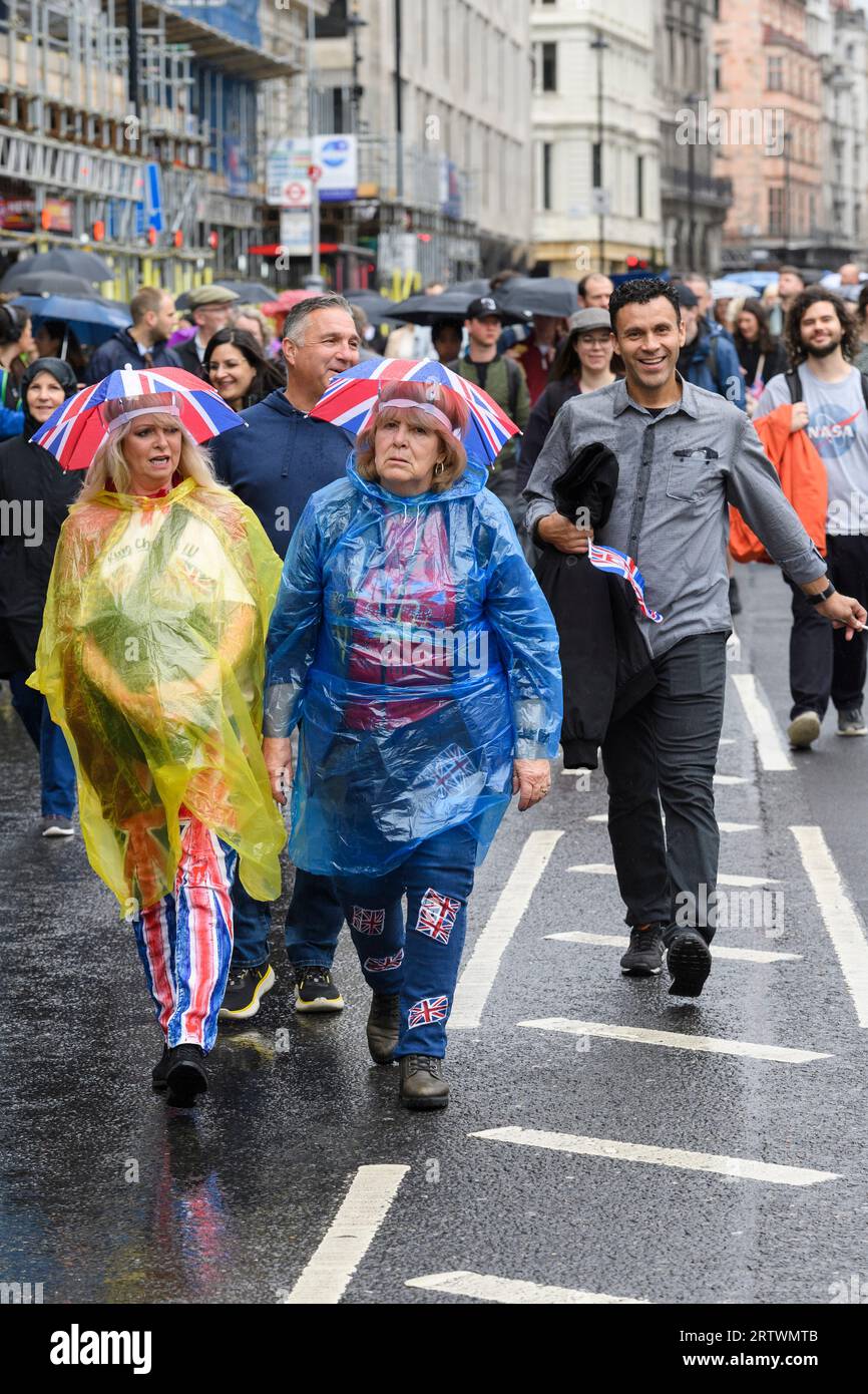 Two women in Union Jack outfits walking along Piccadilly in the rain ...