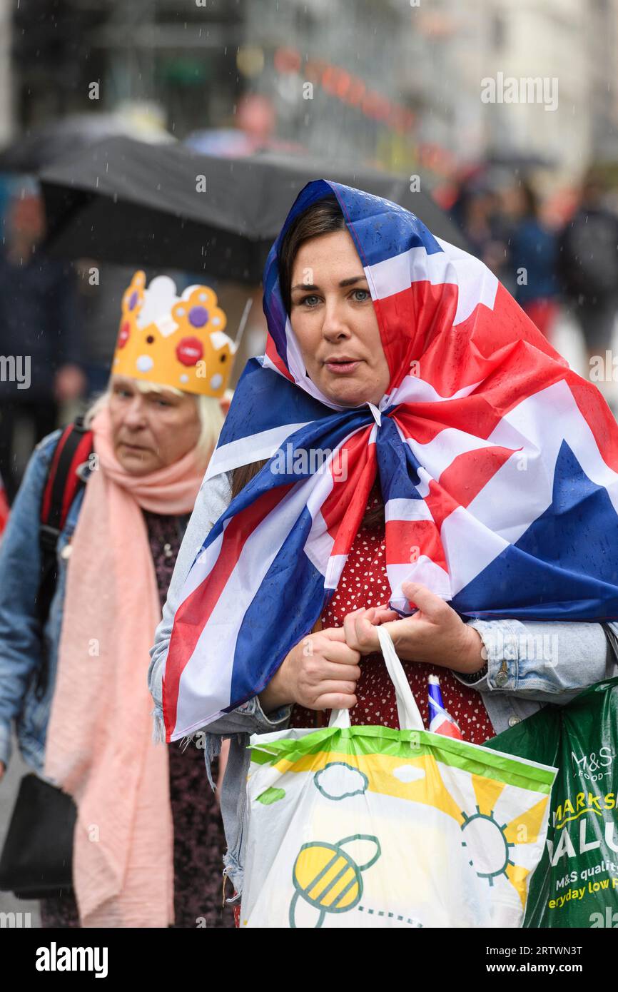 A woman wearing a Union Jack flag walks in the rain along a crowded ...