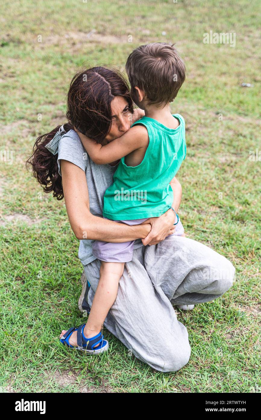 mother and son hugging lovingly on their knees in a green park outdoors ...