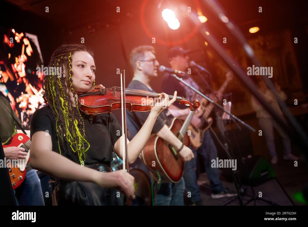 A female violinist plays the violin. Band performs on stage, rock music ...