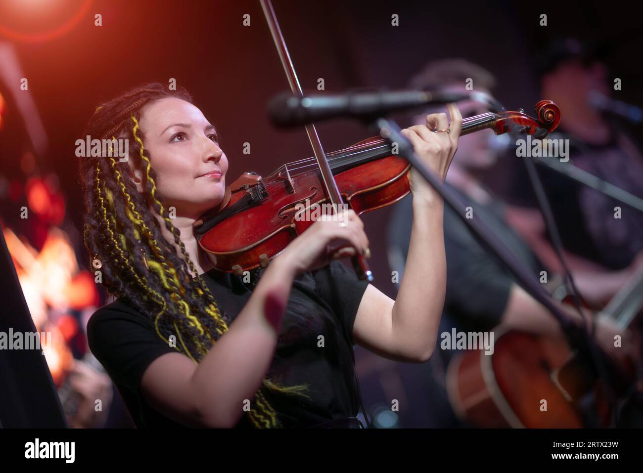 A female violinist plays the violin. Band performs on stage, rock music ...