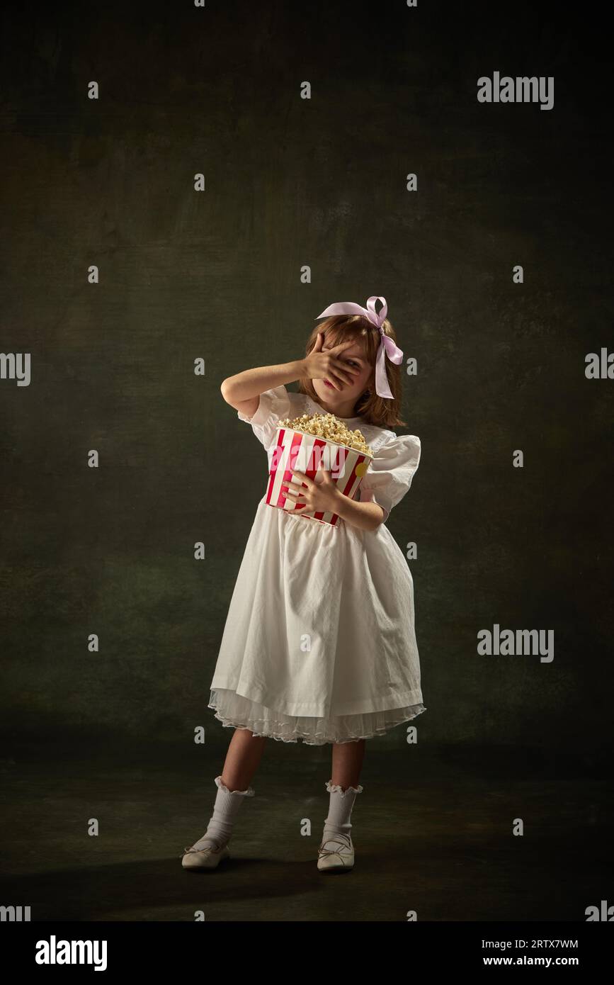 Portrait of scared girl with bucket of popcorn over vintage background ...