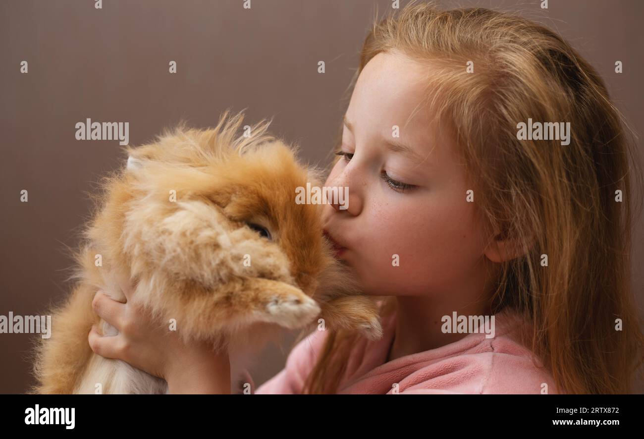 Beautiful young smiling girl is hugging a little red rabbit; child and ...