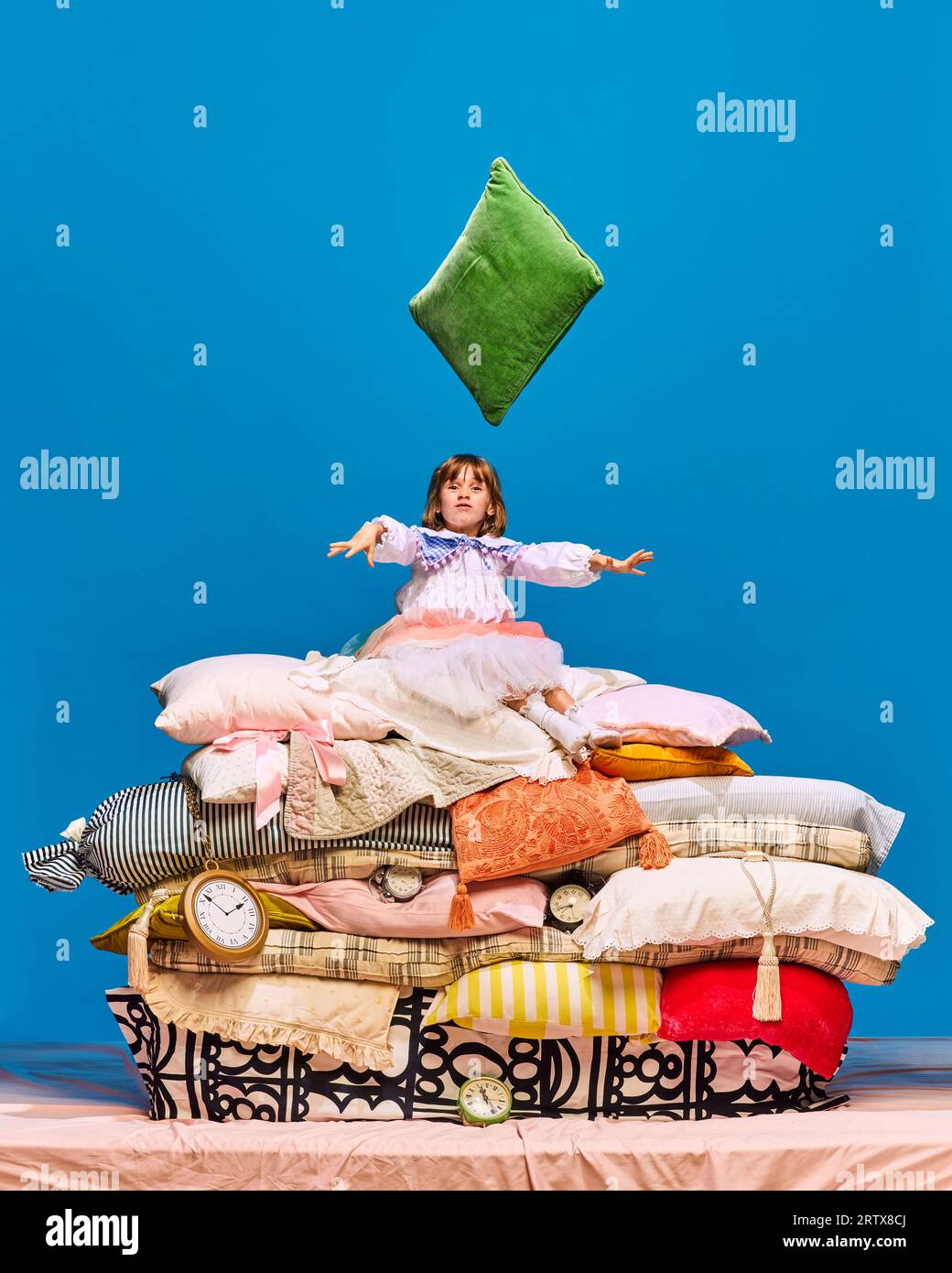 Portrait of little princess on big feather bed and playing with pillows ...