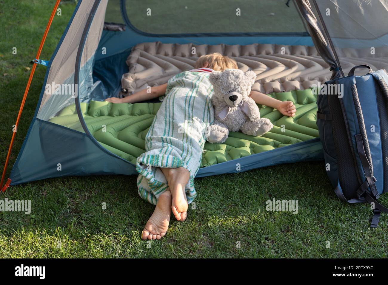 tired barefoot child sleeps or rests lying on his stomach in a tent ...