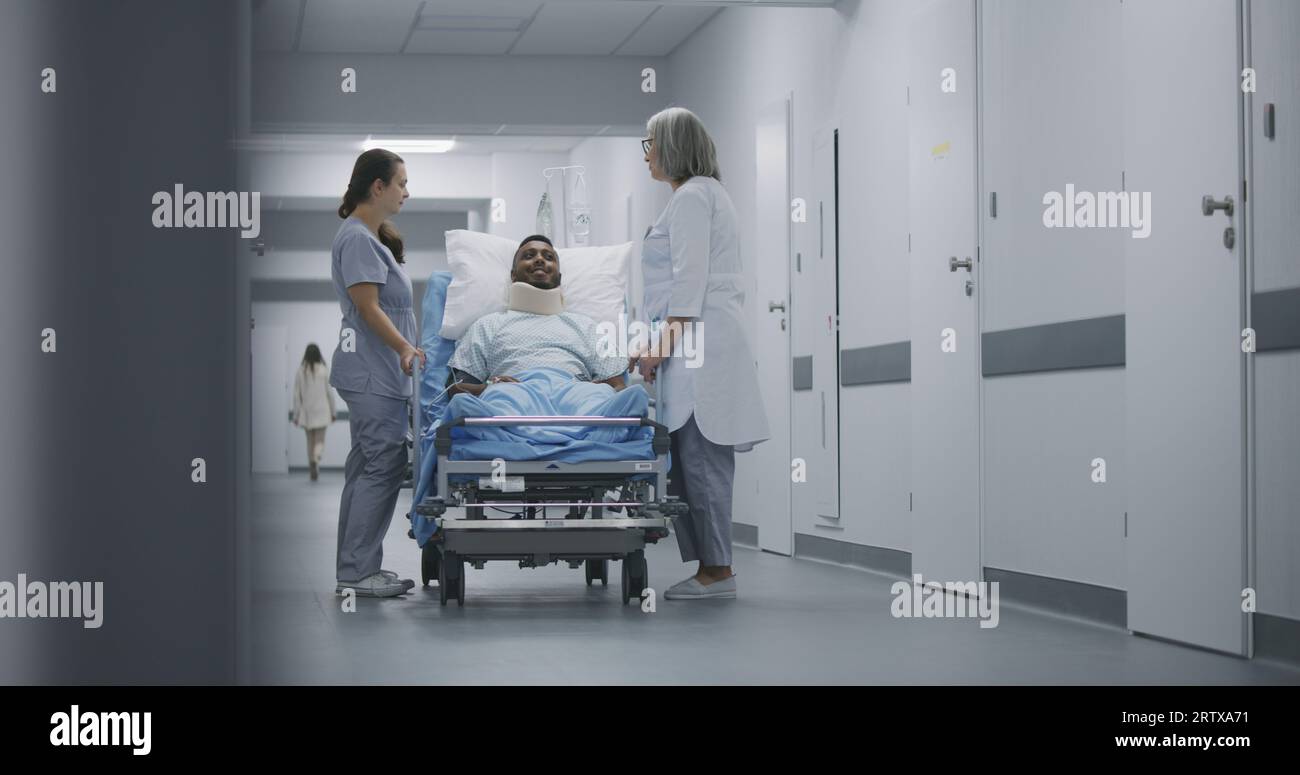 Mature medic and nurse walk down the clinic corridor with injured ...