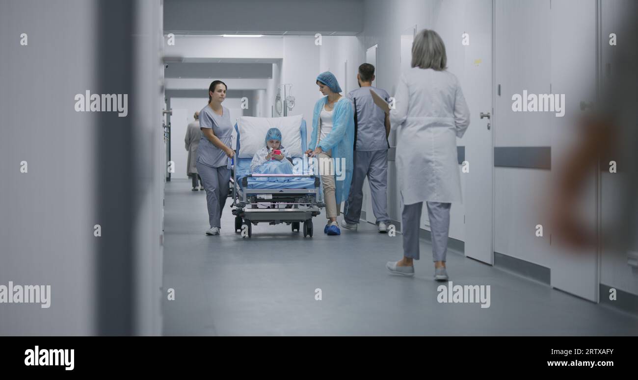 Nurse and mother of child push gurney with young girl in clinic hallway ...