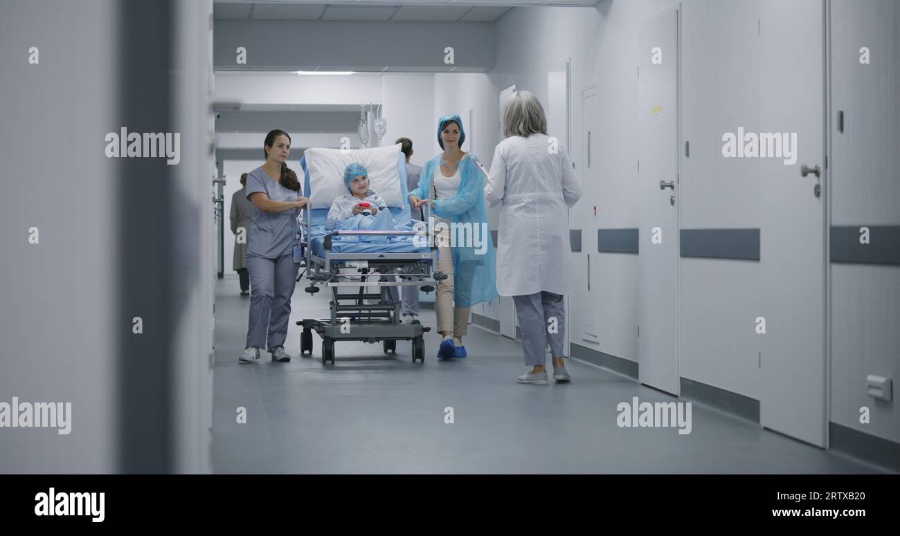 Nurse and mother of child push gurney with young girl in clinic hallway ...