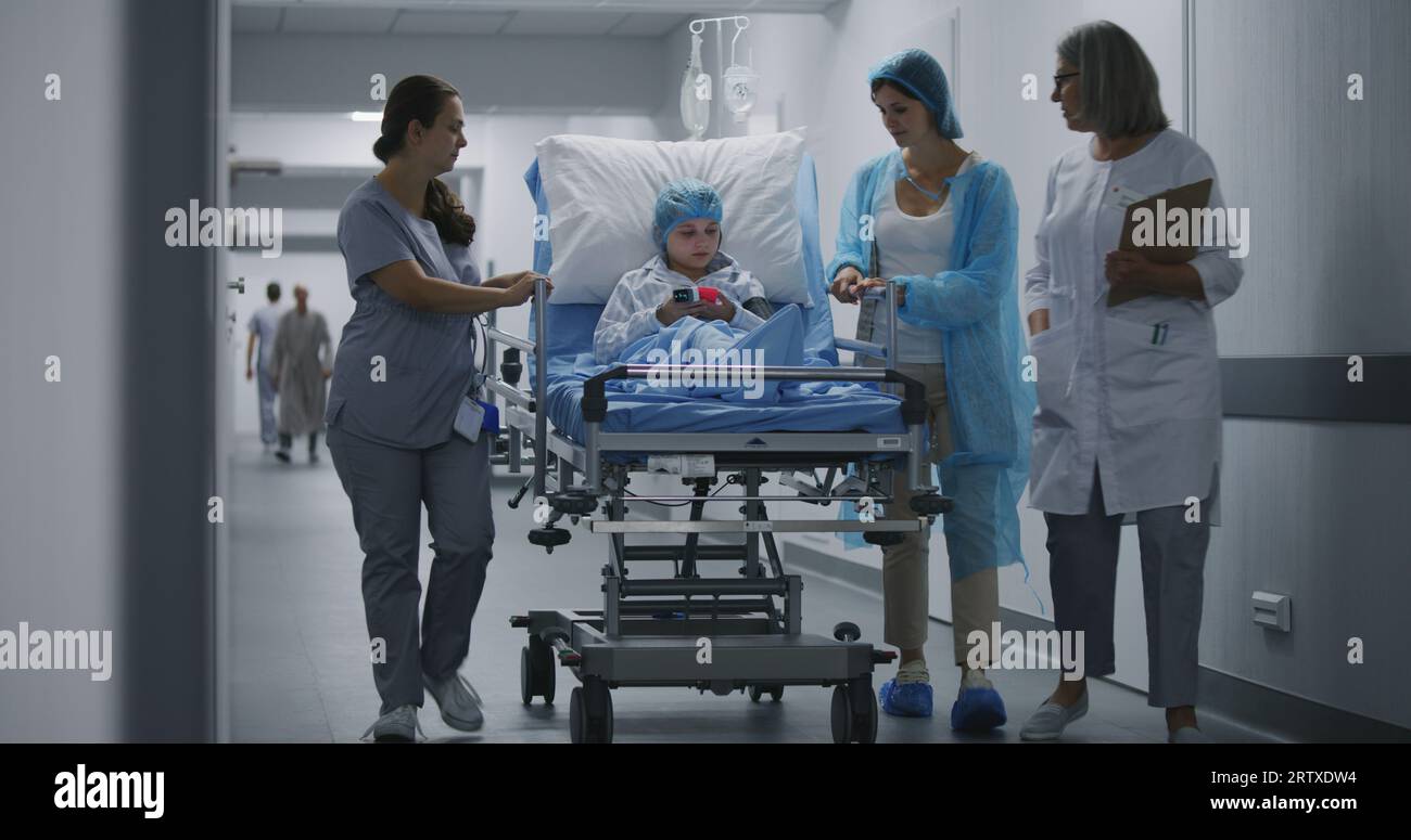 Nurse and mother of child push gurney with young girl in clinic hallway ...