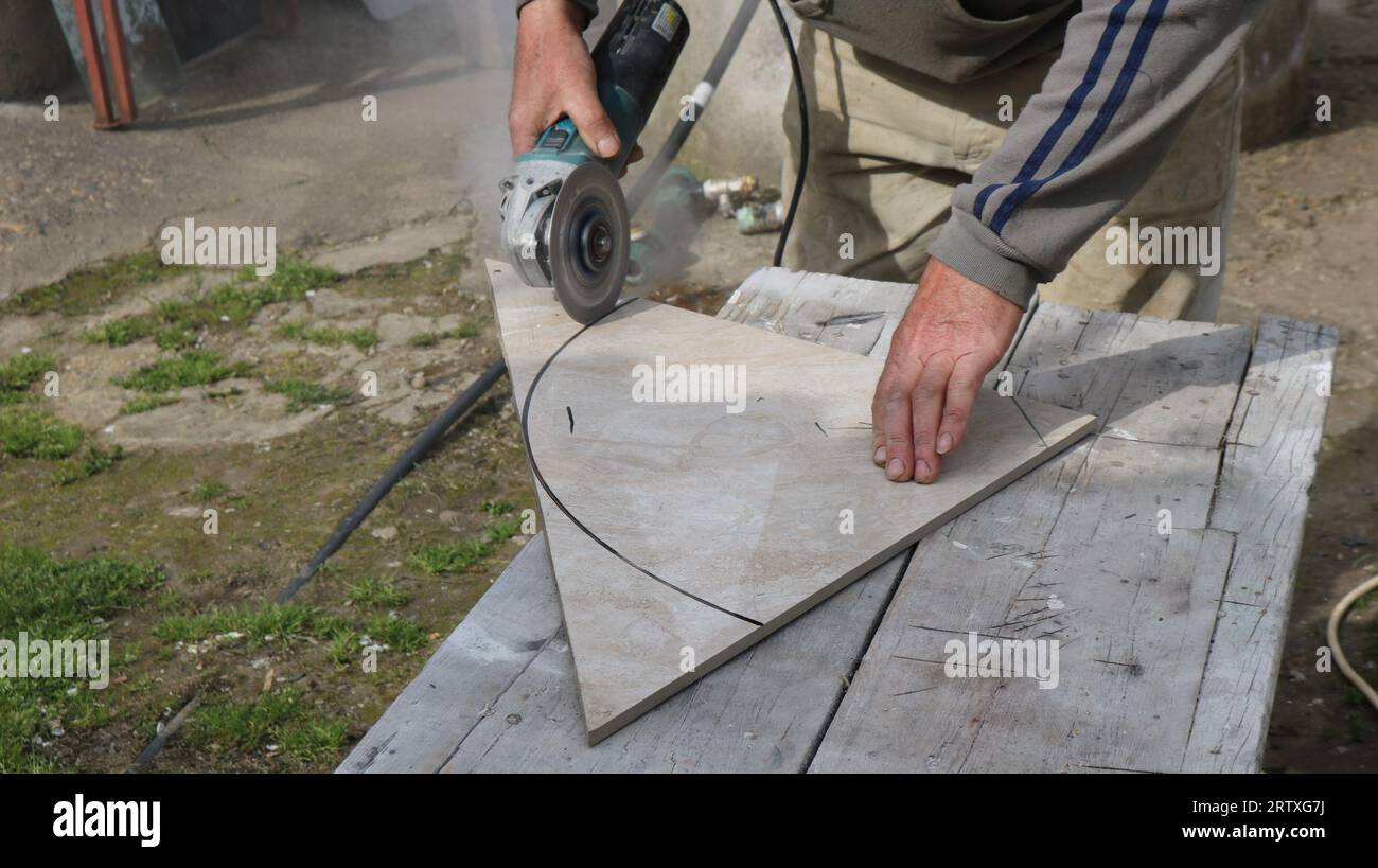 cutting large ceramic tiles with a grinder along a black oval outline ...