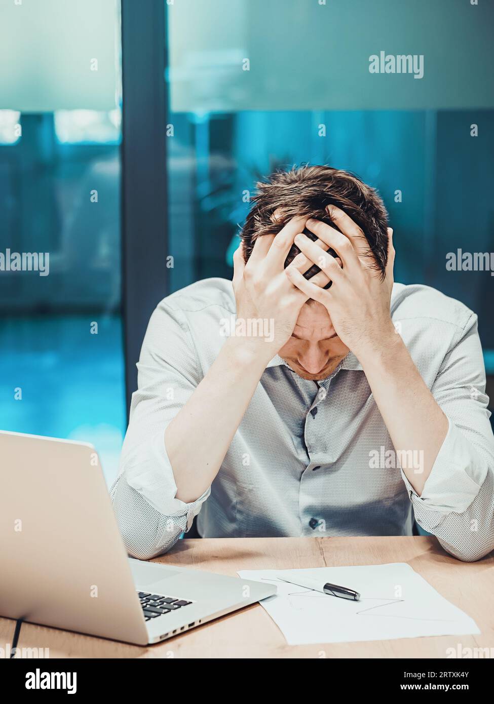 Office worker sits at table and holds his head in his hands. Depression ...