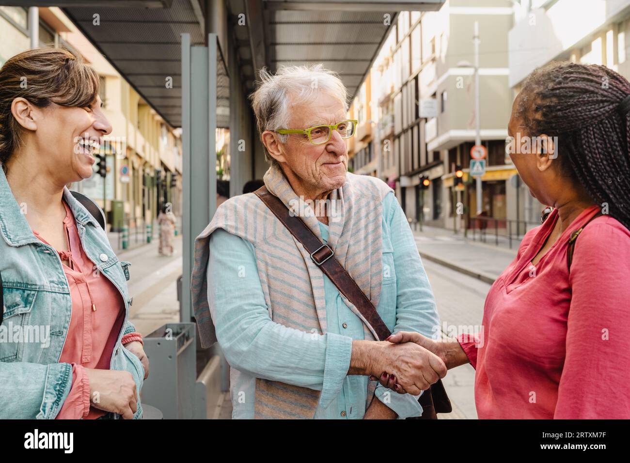 Happy multiracial people talking while waiting at the bus station in ...