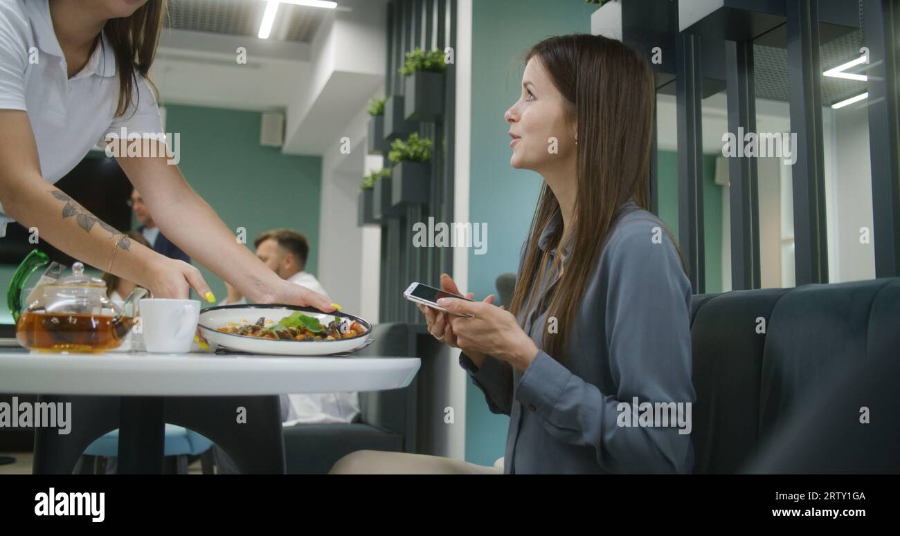 Woman sits at the table in clinic cafe, uses phone. Cafeteria worker ...
