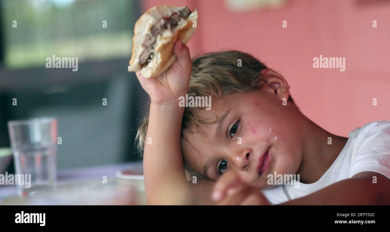 Cute bored toddler boy eating hamburger for lunch. Child eats burger ...